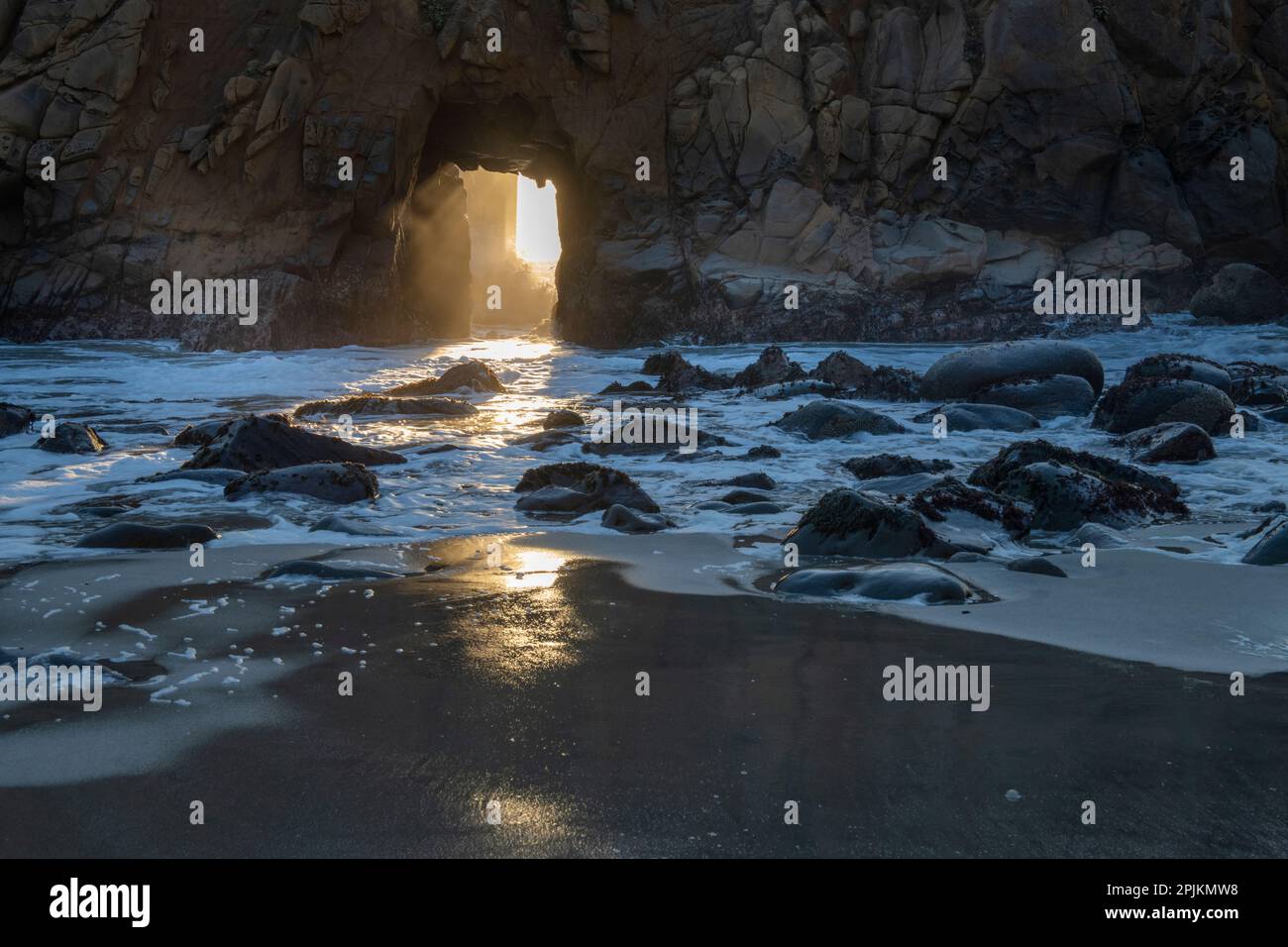 Sun shines through a tunnel in a sea cliff in the Big Sur area Stock ...