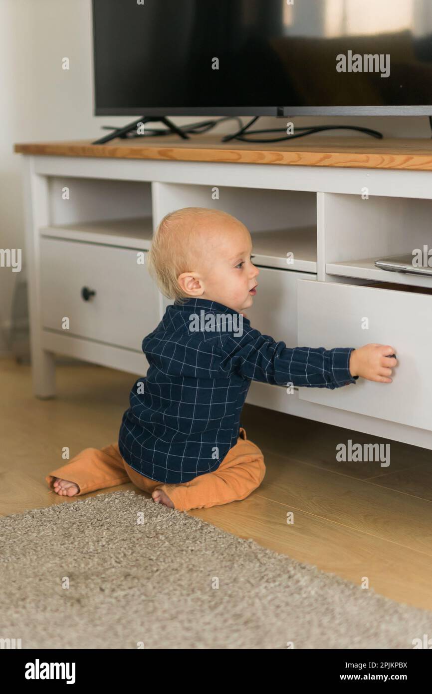 Toddler baby boy open cabinet drawer with his hand. Child explore what ...