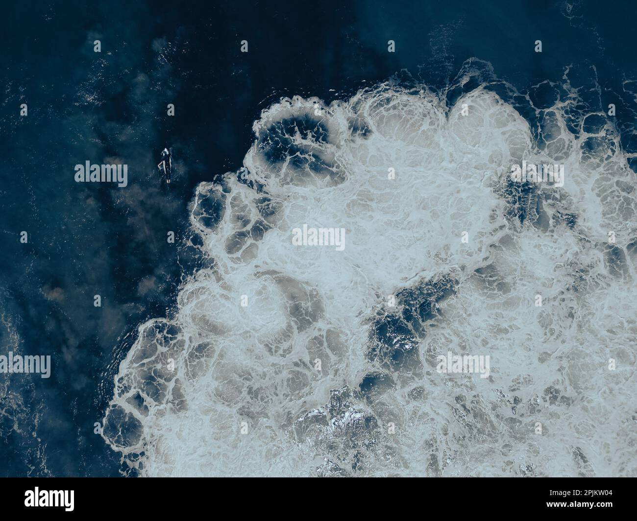 An aerial view of a surfer on a surfboard in the middle of a bright ...