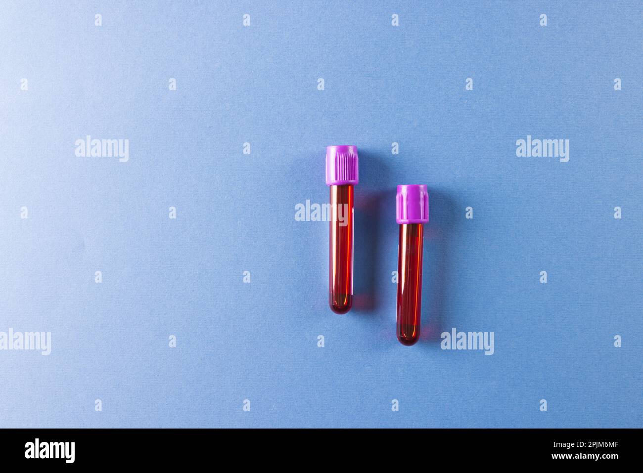 Two blood sample tubes with purple lids, on blue background with copy ...