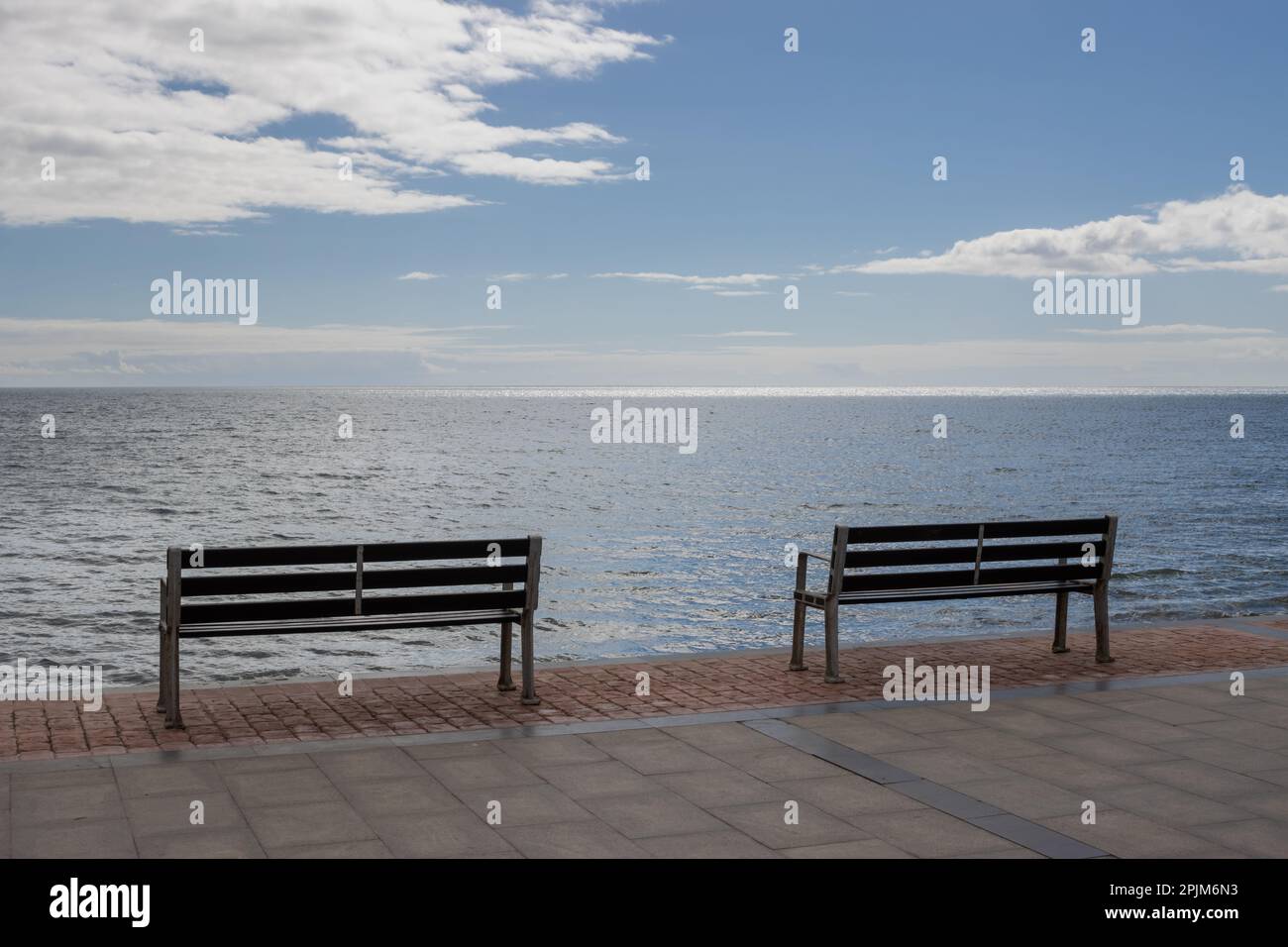 Promenade at the coast of the Atlantic ocean. Two empty benches to ...