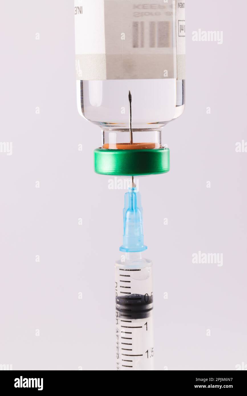 Syringe filling from vial of clear liquid such as insulin, on white ...