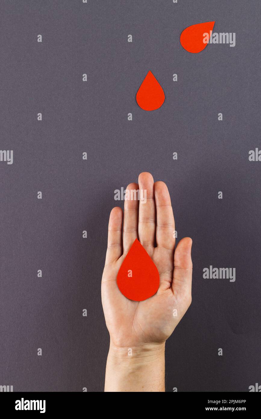 Hand of caucasian woman holding blood drop, with blood drops on grey ...