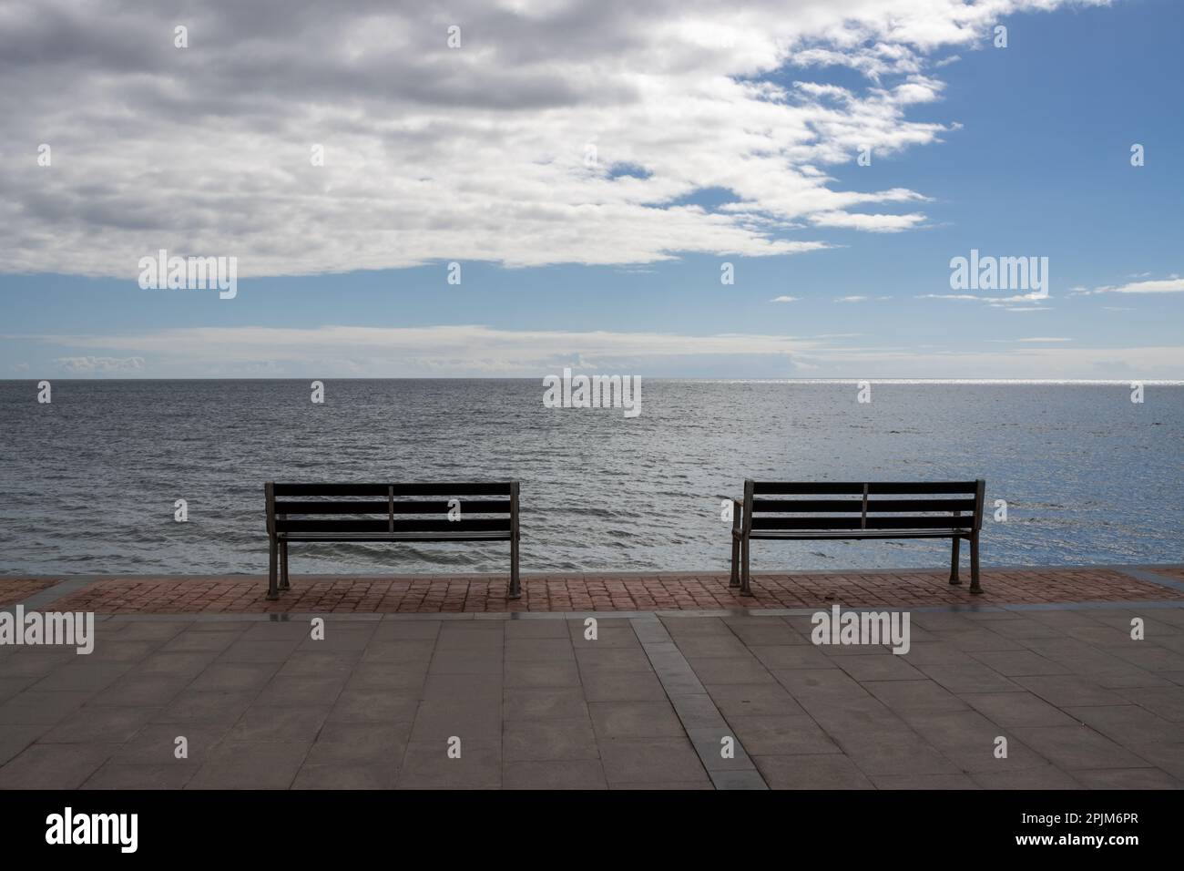 Promenade at the coast of the Atlantic ocean. Two empty benches to ...