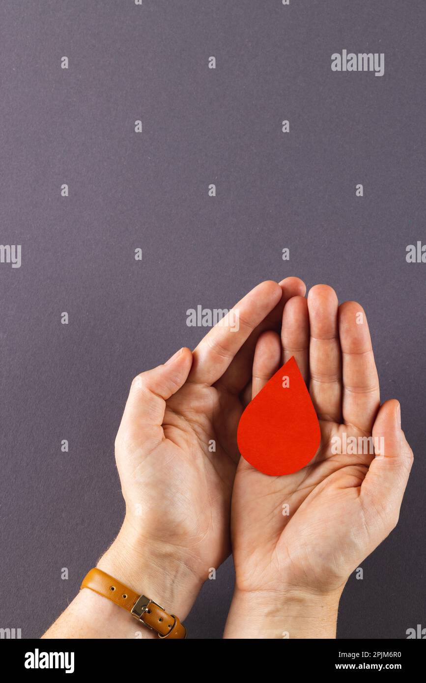 Hands of caucasian woman cupping blood drop, on grey background with ...
