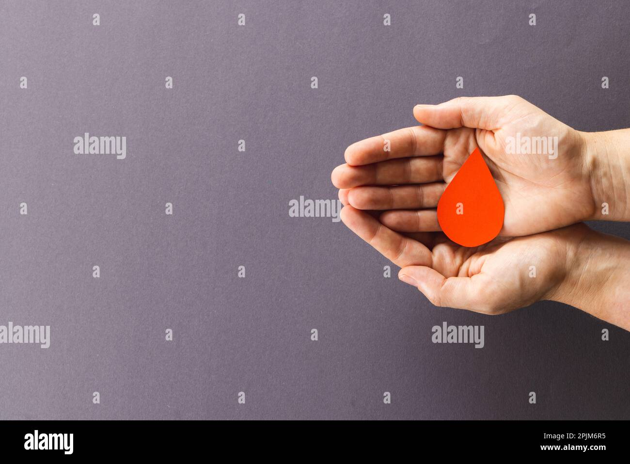 Hands of caucasian woman cupping blood drop, on grey background with ...