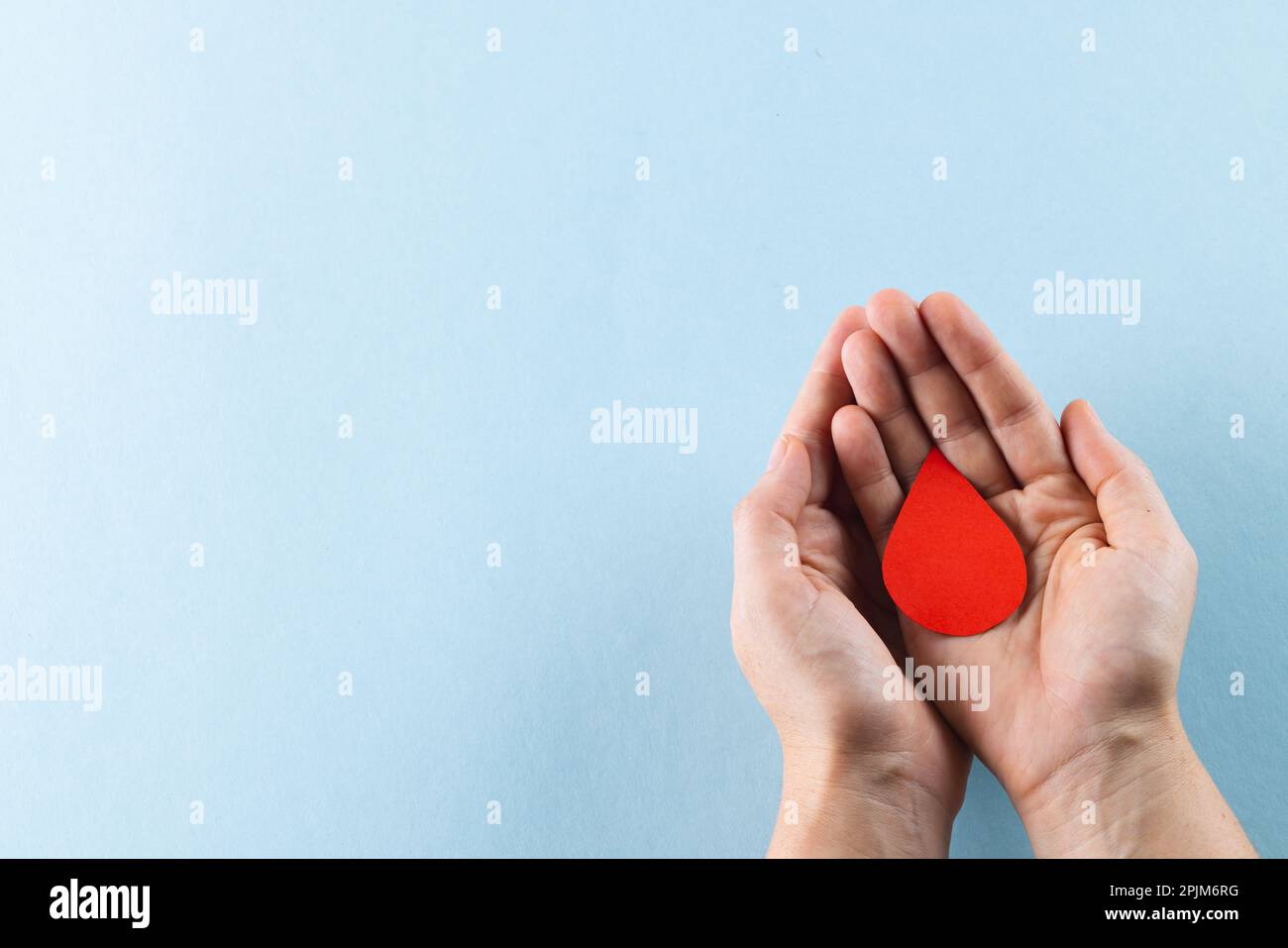 Hands of caucasian woman cupping blood drop on blue background with ...