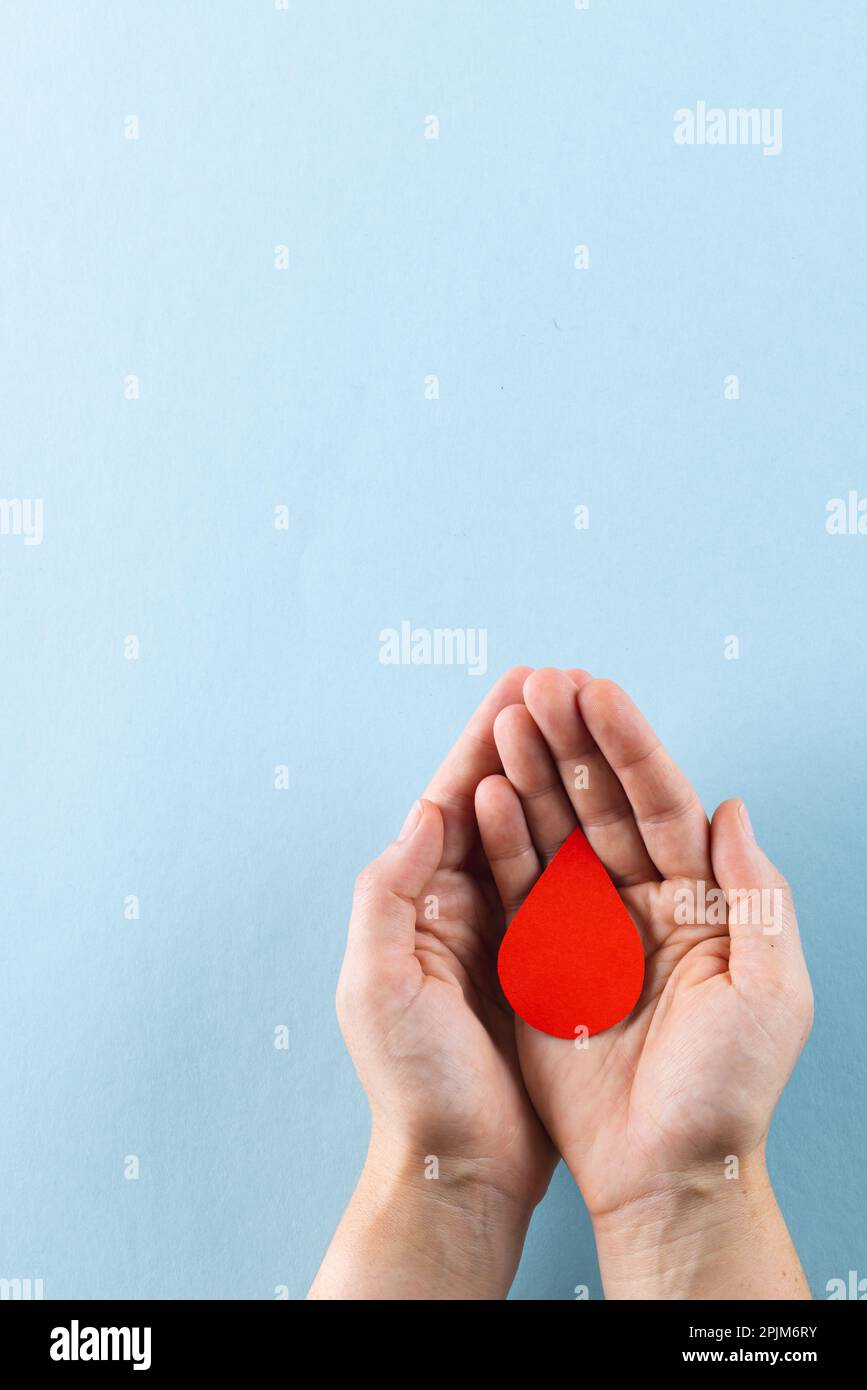 Hands of caucasian woman cupping blood drop on blue background with ...