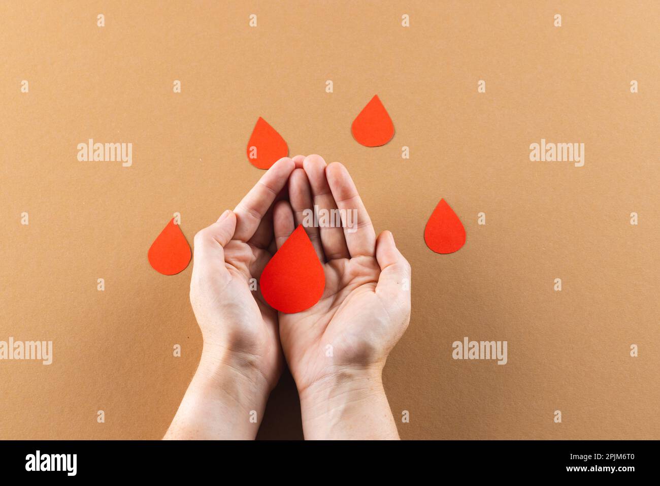 Hands of caucasian woman cupping blood drop, with blood drops on brown ...