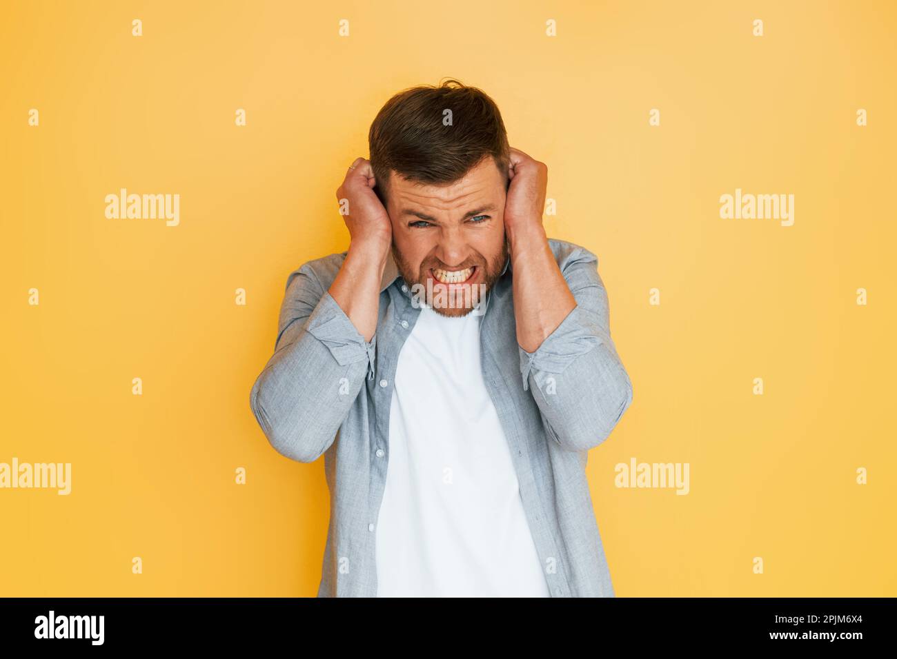 Headache and anger. Young man in casual clothes standing indoors in the ...