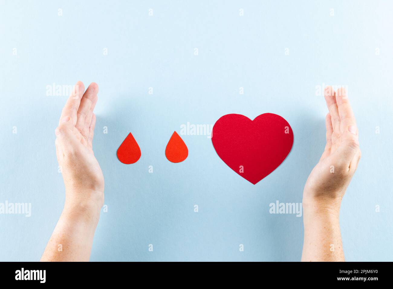 Hands of caucasian woman protecting blood drops and heart on blue ...