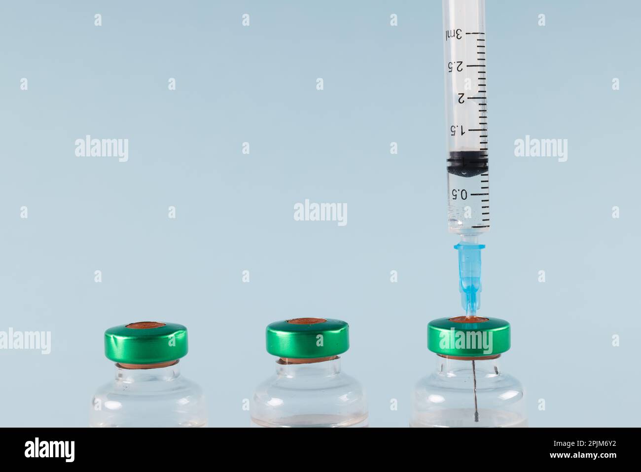 Three vials with syringe filling from one, on blue background with copy ...