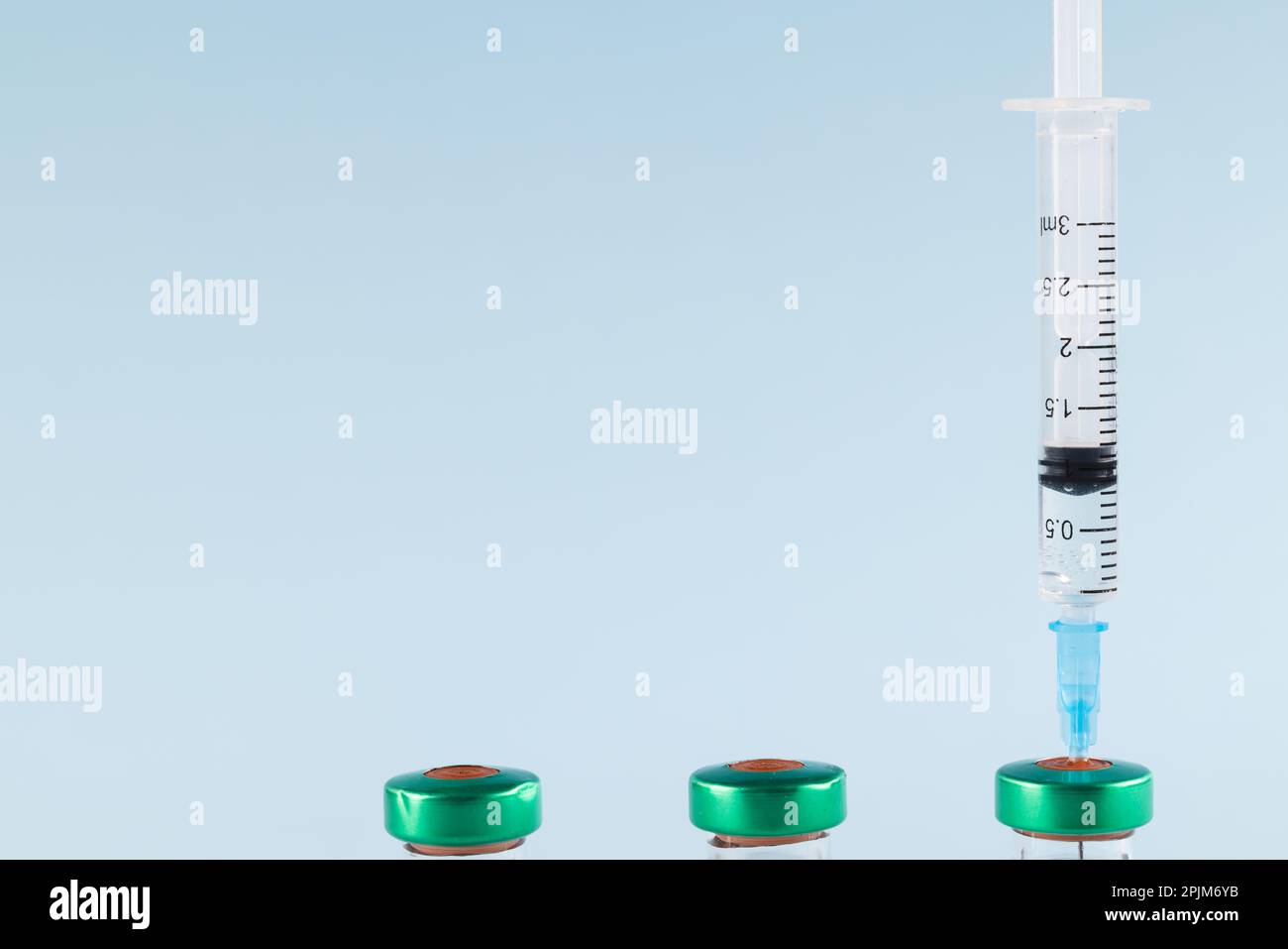 Three vials with syringe filling from one, on blue background with copy ...