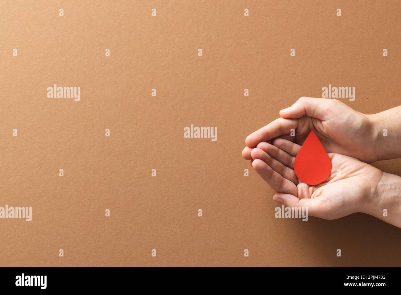 Hands of caucasian woman cupping blood drop, on brown background with ...