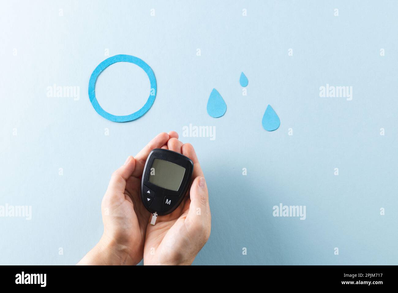 Hands of caucasian woman holding glucometer over blue drops and ring on ...