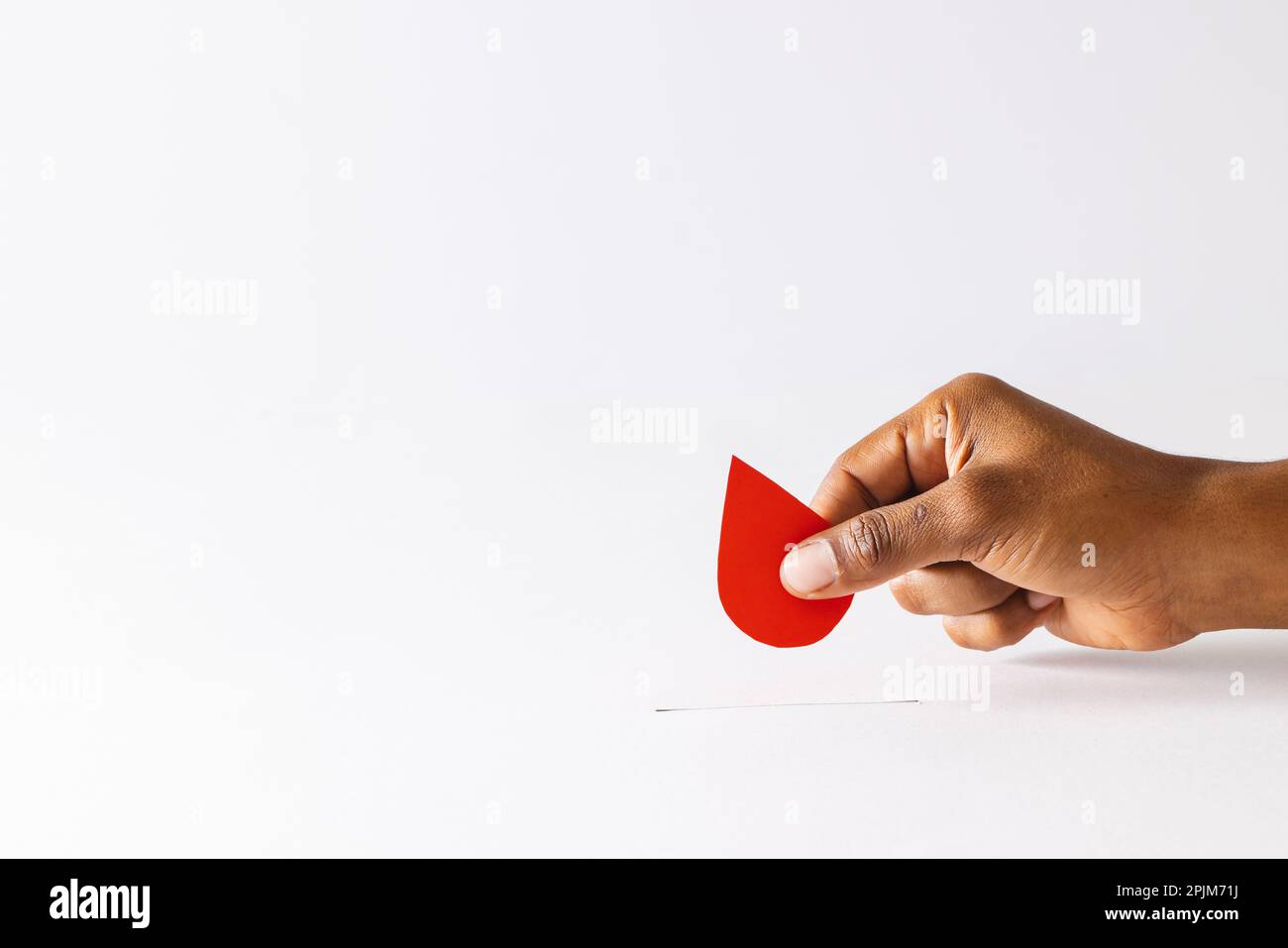 Hand of biracial man holding blood drop above slot, on white background ...