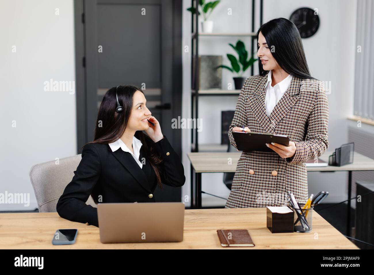 Call center agent with headset working on support hotline in modern office. Two young attractive ...