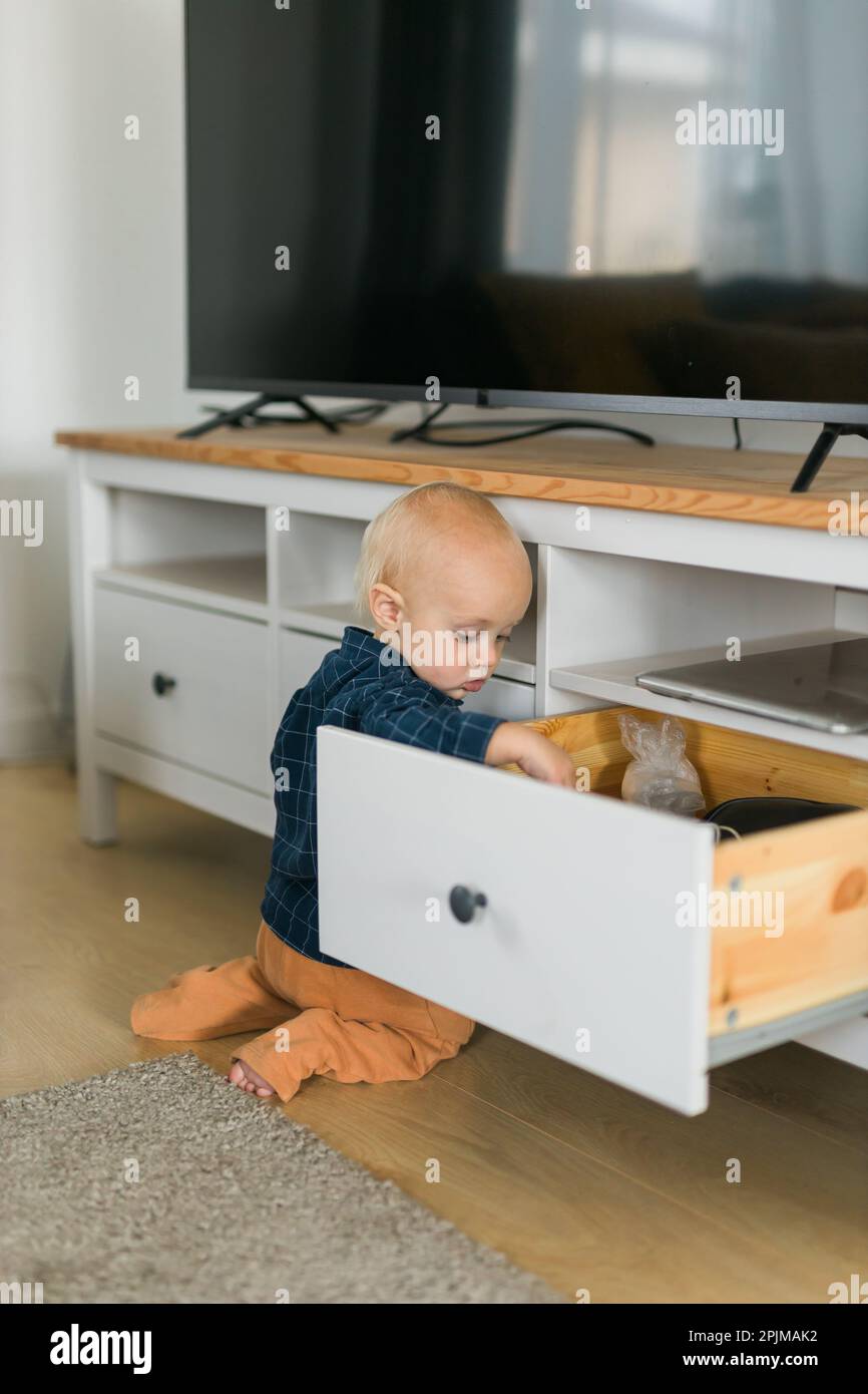 Toddler baby boy open cabinet drawer with his hand. Child explore what ...