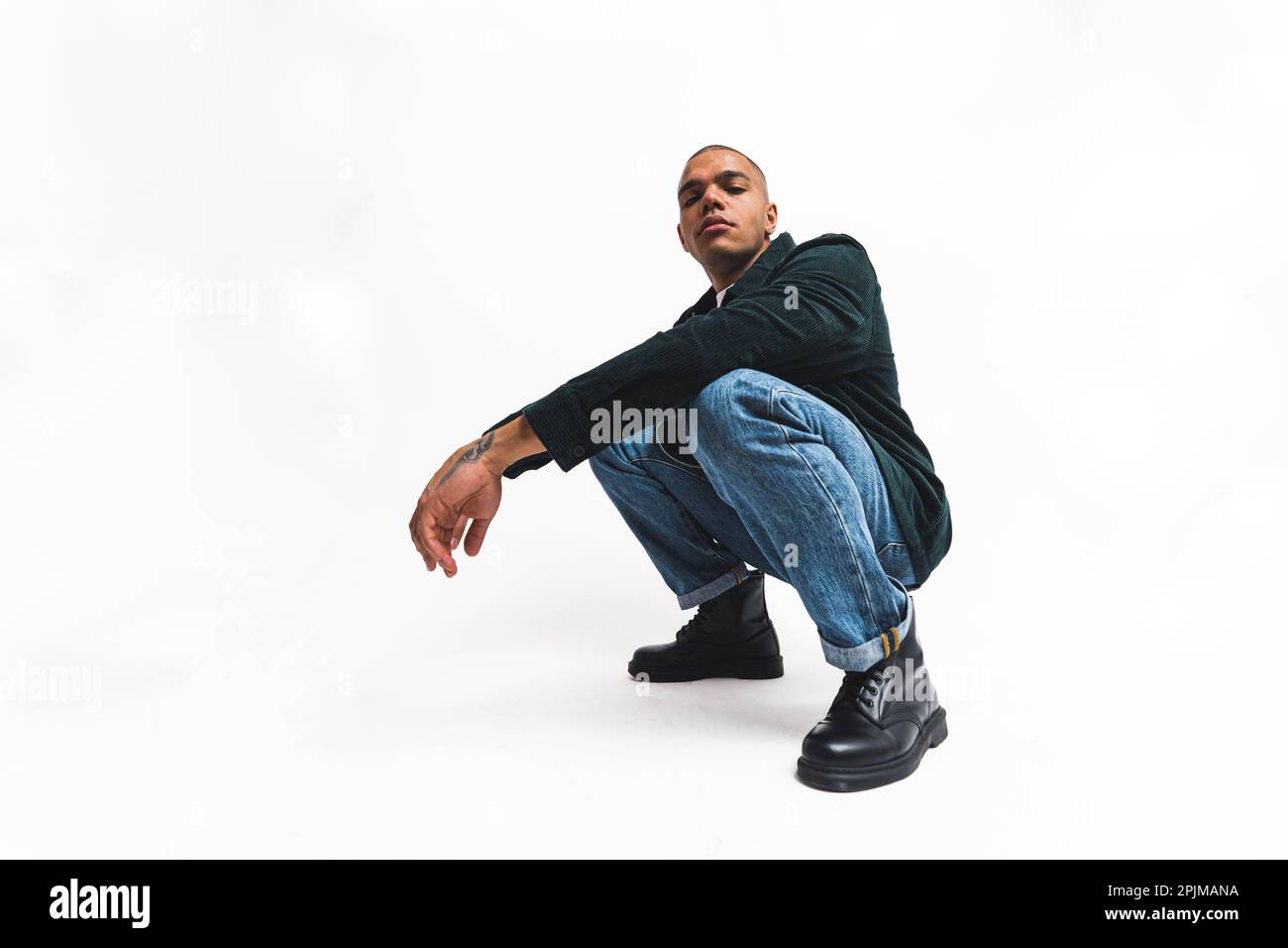 Serious focused male model squatting in studio during fashion ...