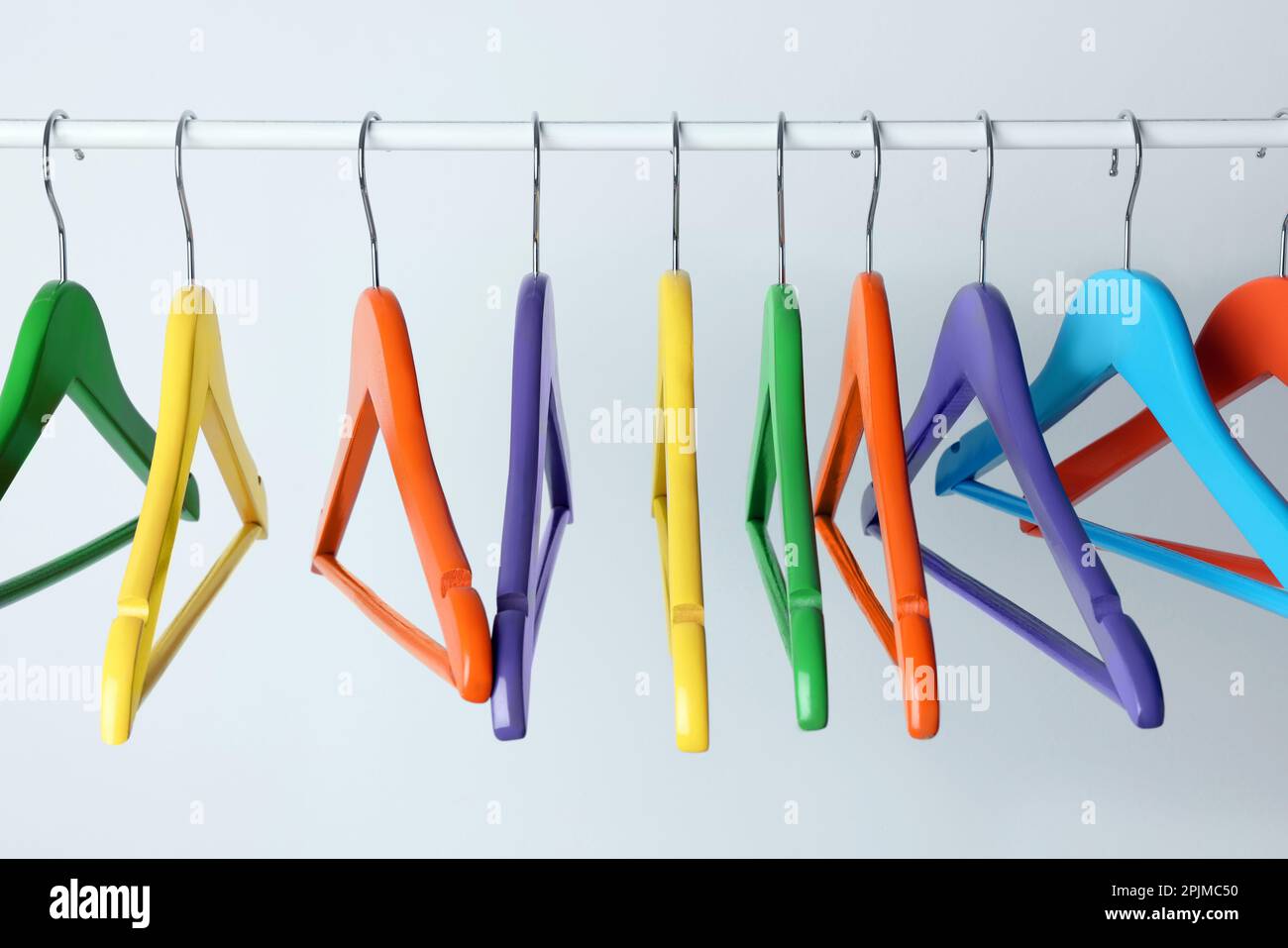 Bright clothes hangers on metal rail against light background Stock ...
