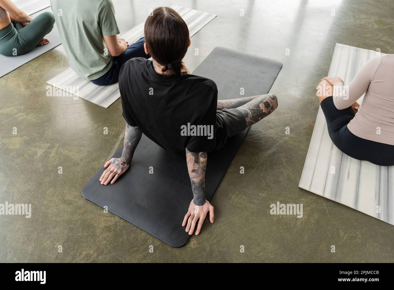 Overhead view of tattooed man sitting on mat near interracial people in ...