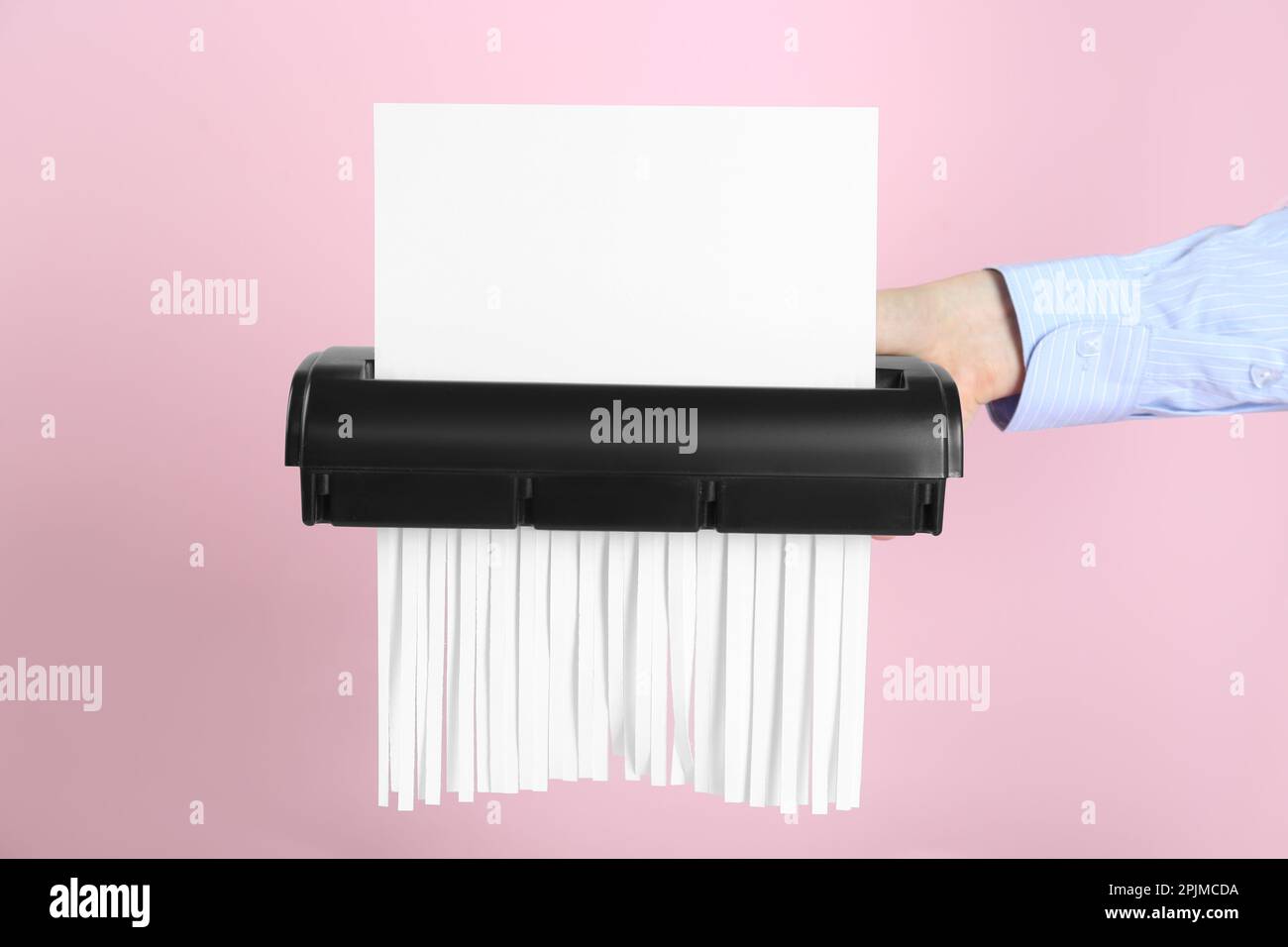 Woman destroying sheet of paper with shredder on pink background ...