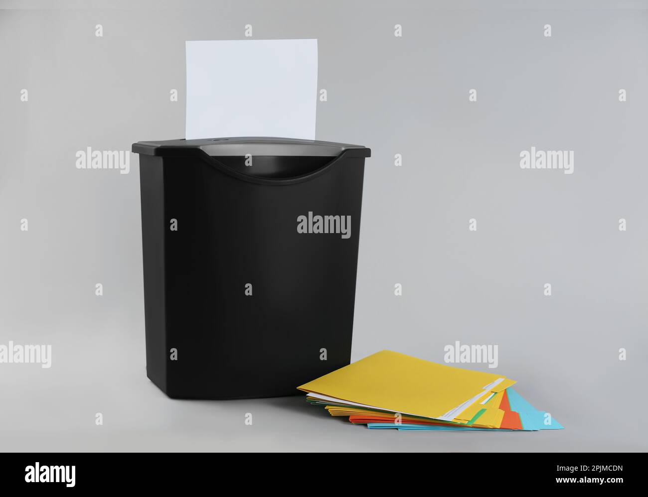 Shredder with sheet of paper and colorful folders on grey background ...