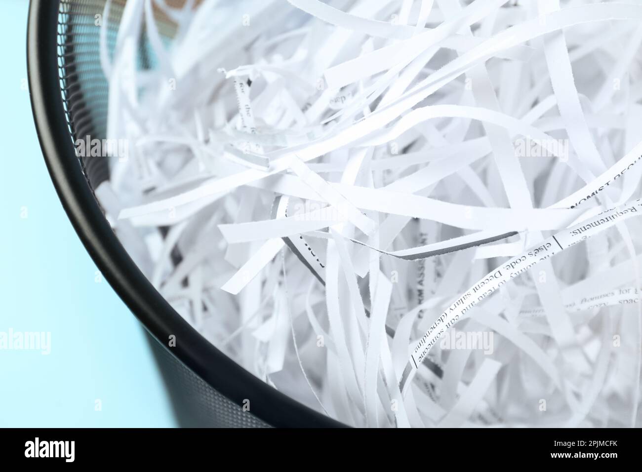 Trash bin with shredded paper strips on light blue background, closeup ...