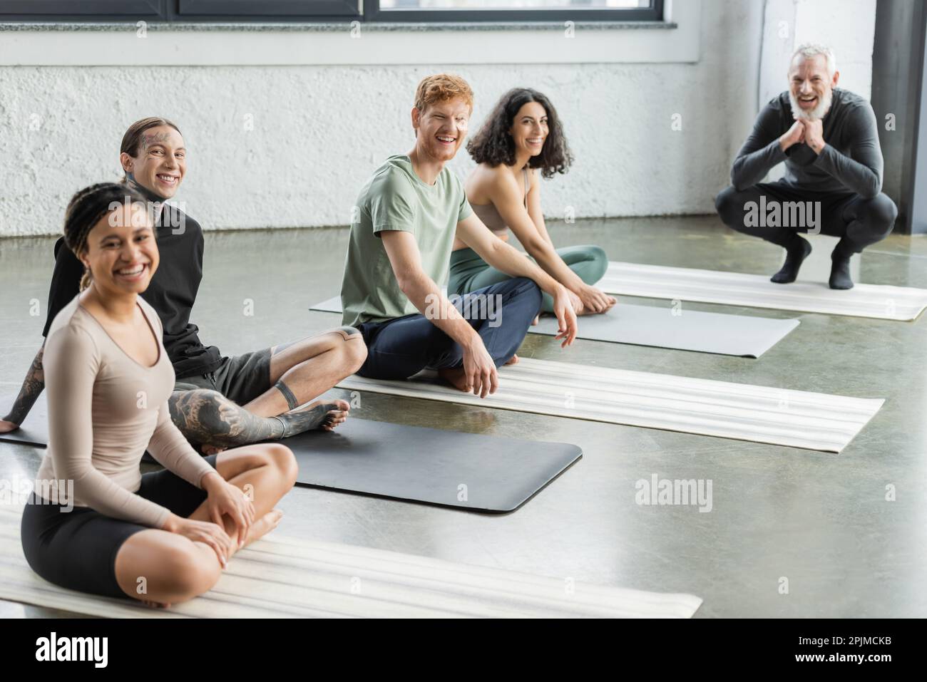 Cheerful multiethnic group and coach looking at camera in yoga studio ...