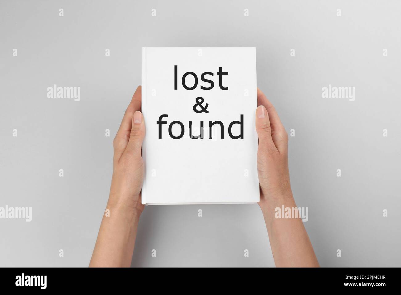 Woman holding book with phrase Lost and Found on light grey background ...