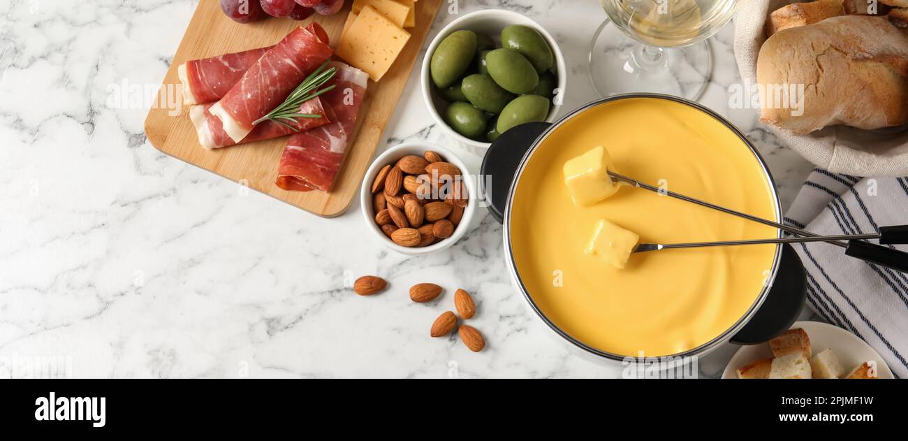 Pot of tasty cheese fondue and snacks on white marble table, flat lay ...