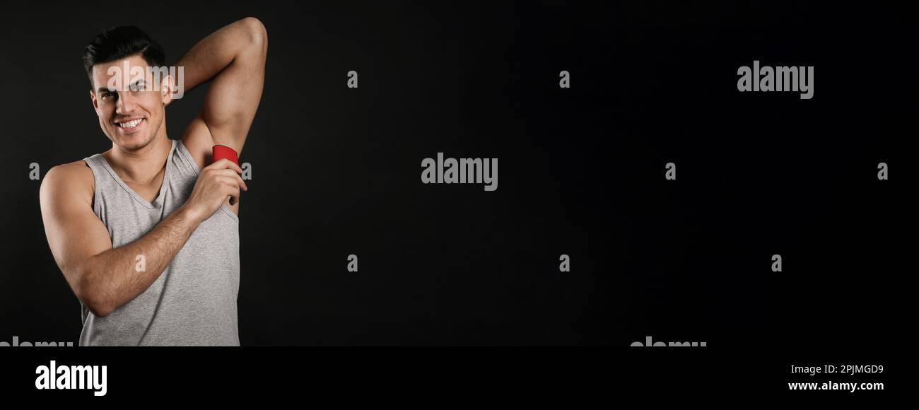 Handsome man applying deodorant to armpit on black background, space ...