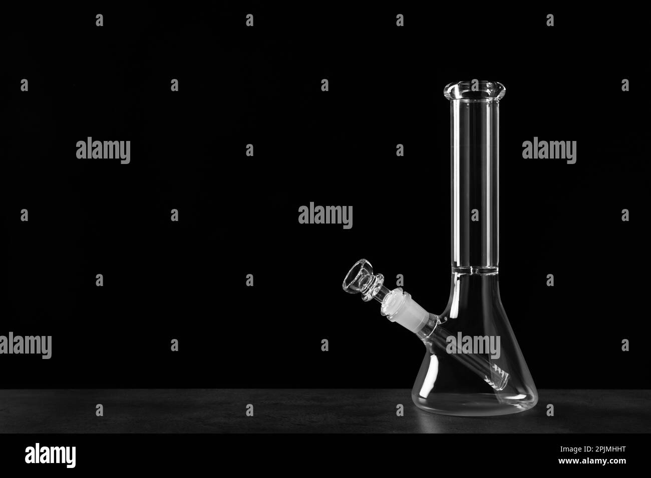 Glass bong on grey table against black background, space for text ...