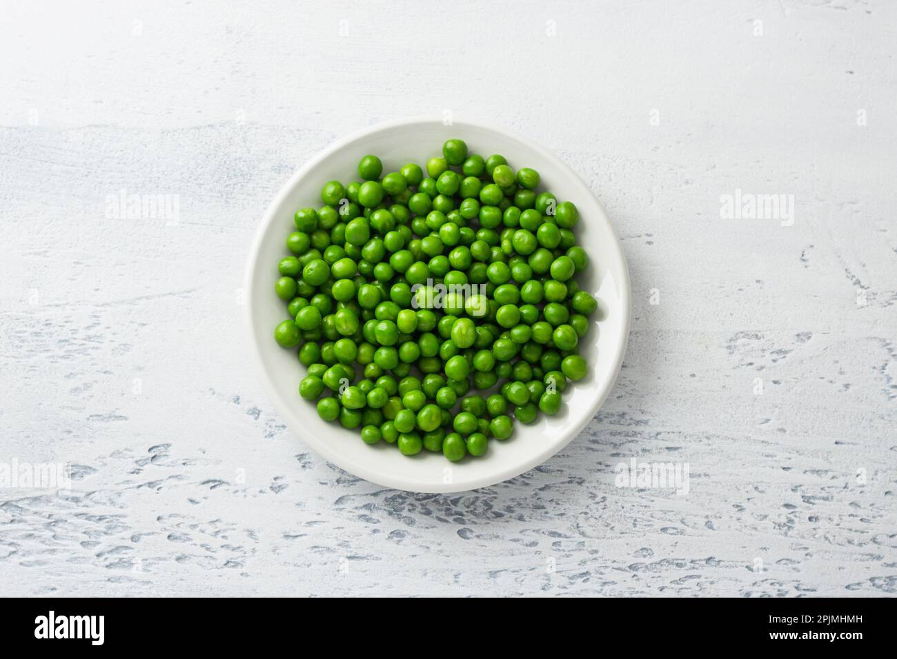 White plate with steamed green peas on a light blue background, flat ...