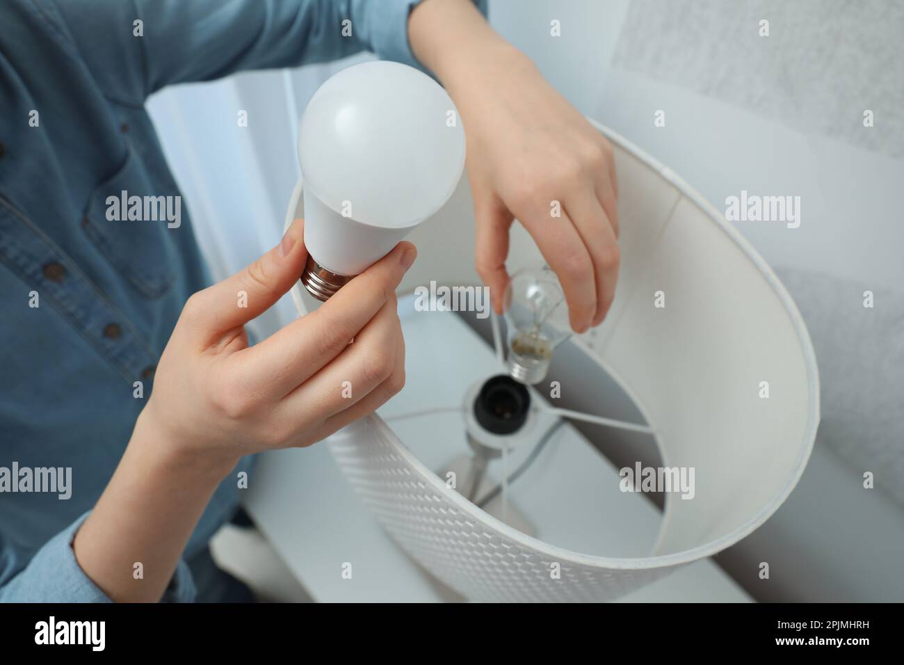 Woman changing incandescent light bulb for fluorescent one in lamp at ...