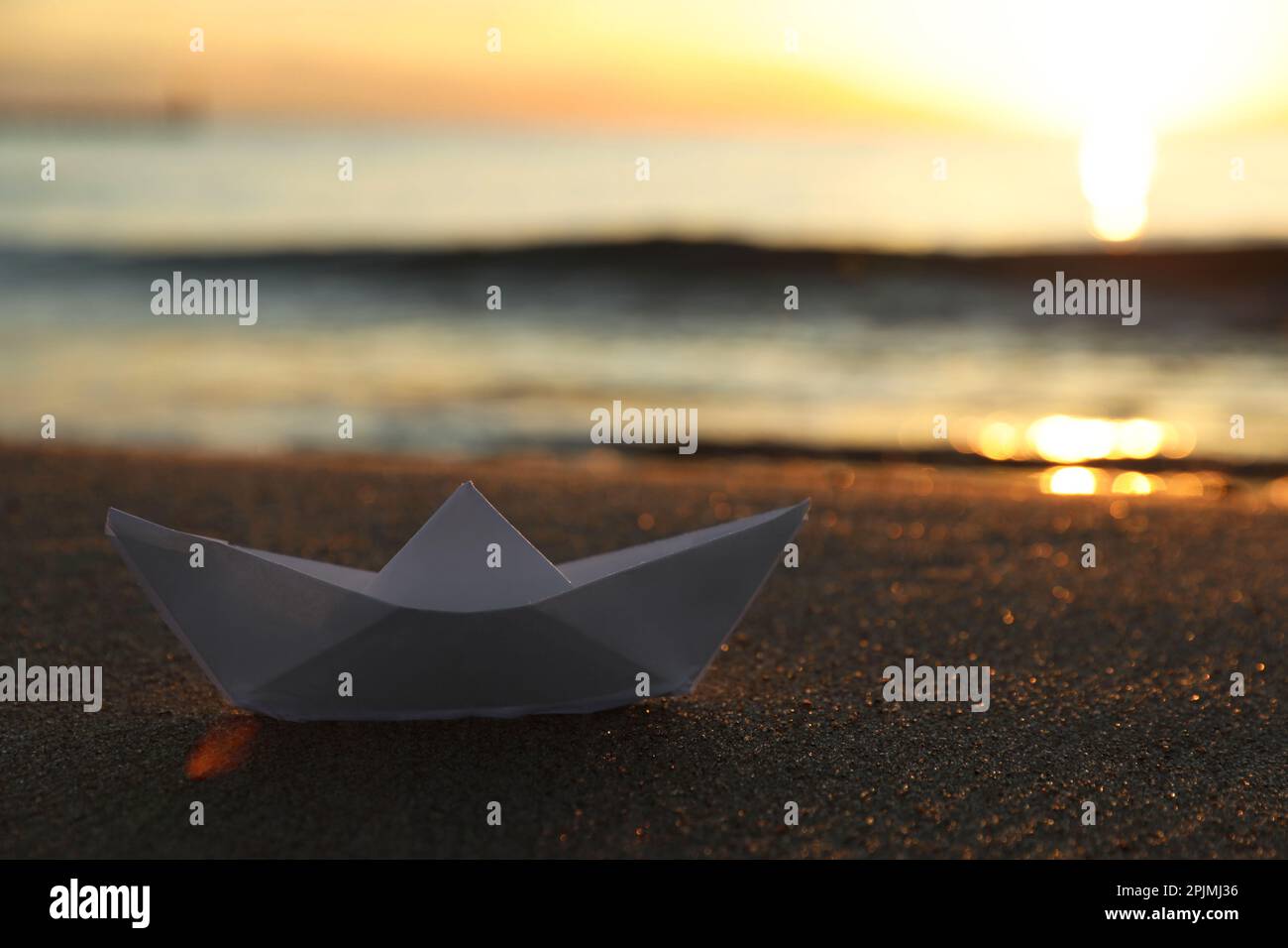 White paper boat on sand near sea at sunset, closeup. Space for text ...