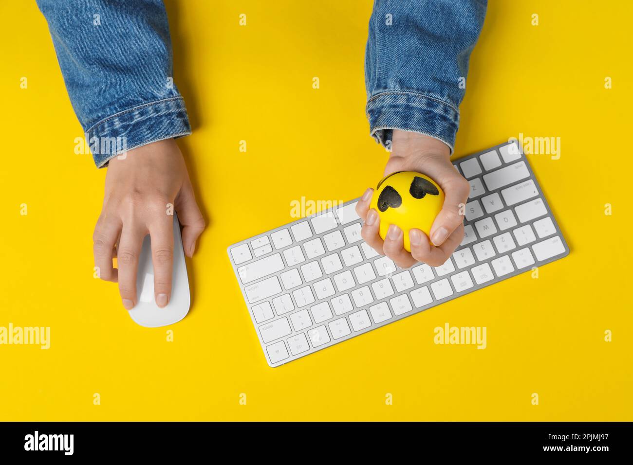 Woman squeezing antistress ball while working with computer on yellow ...