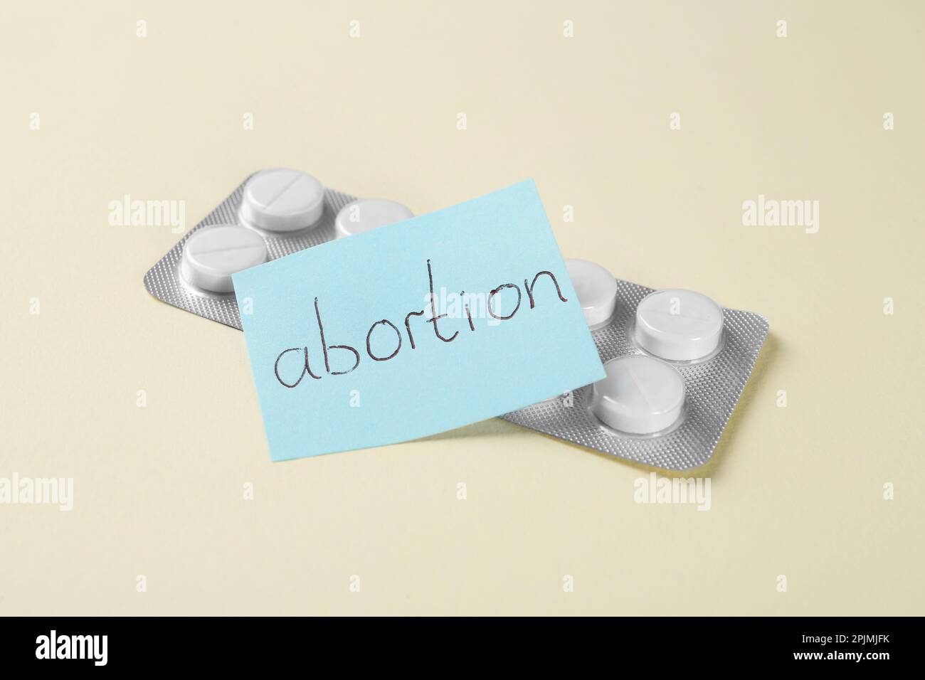 Paper note with word Abortion and pills on beige background, closeup ...
