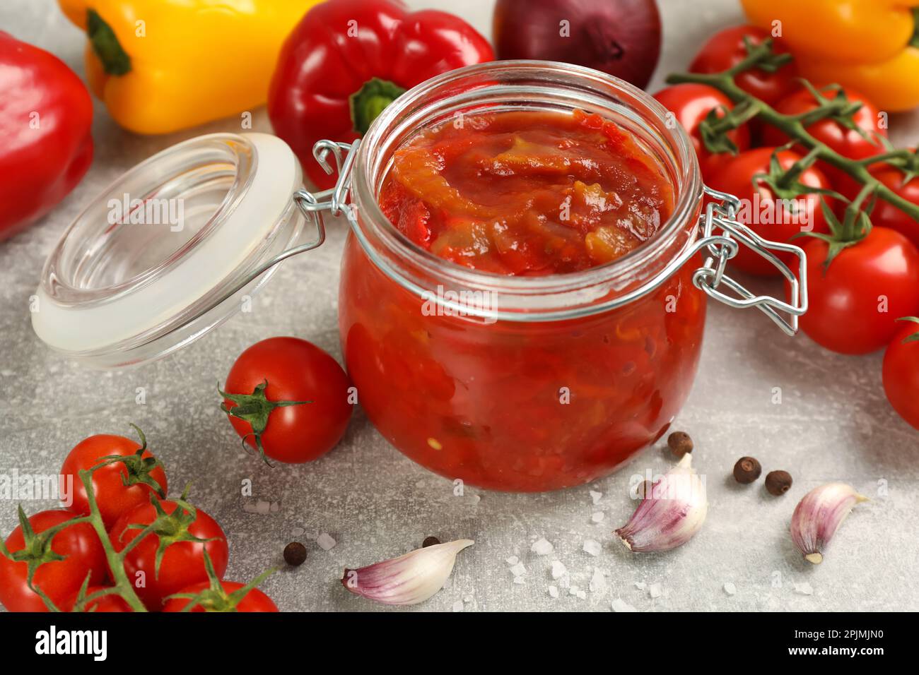 Glass jar of delicious canned lecho and fresh ingredients on light grey ...
