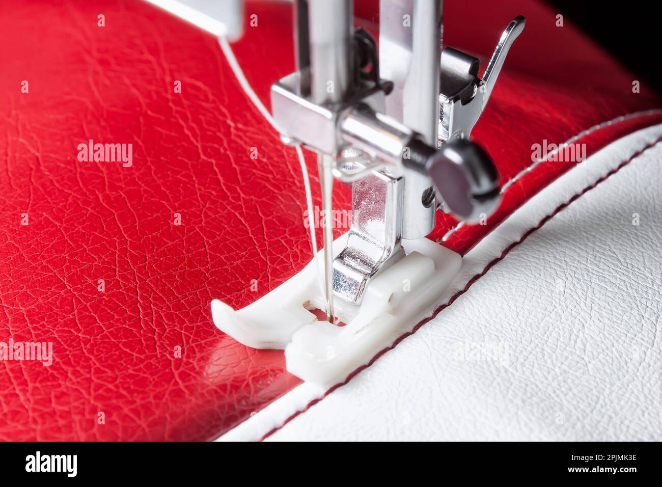 Modern sewing machine presser foot makes a seam on white and red ...