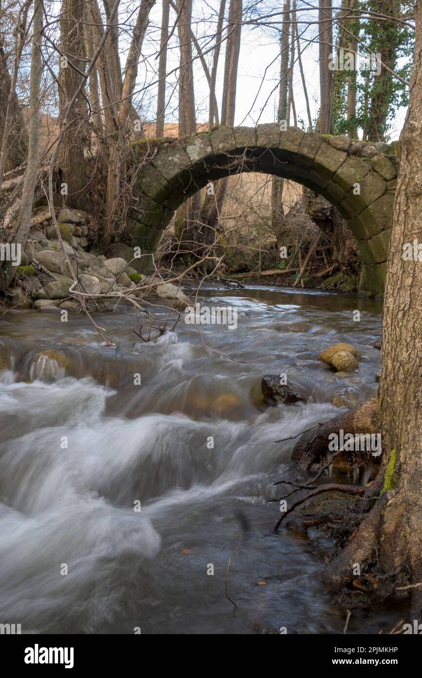 Small round stone bridge with moss over small fast flowing mountain ...
