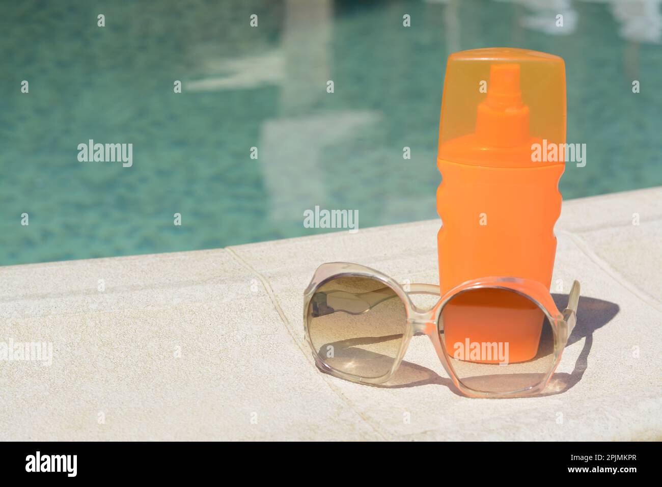Stylish sunglasses and sunscreen near outdoor swimming pool on sunny ...