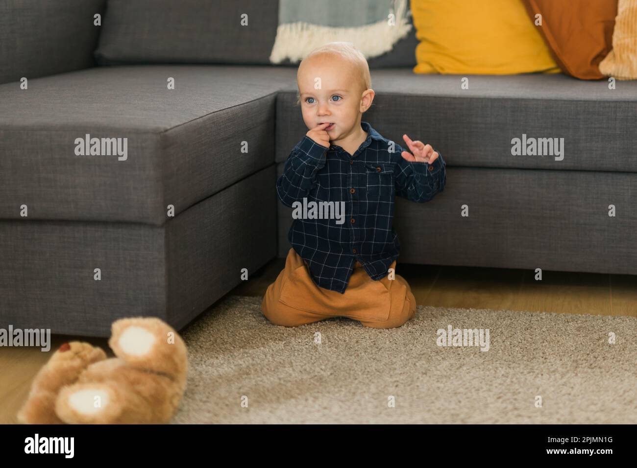 Surprised baby sitting on carpet. Child's eyes widened and mouth opened ...