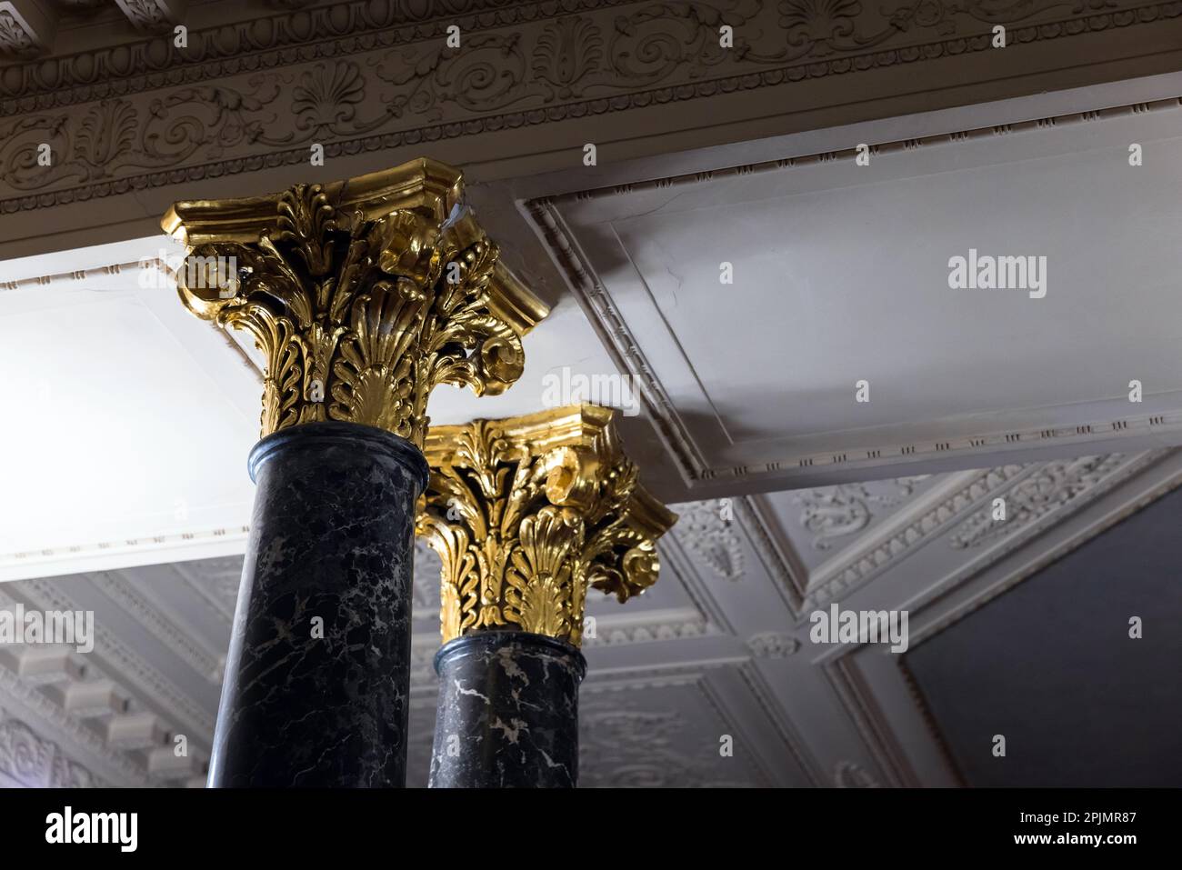 Stone pillars with gold colored capitals are under white ceiling ...