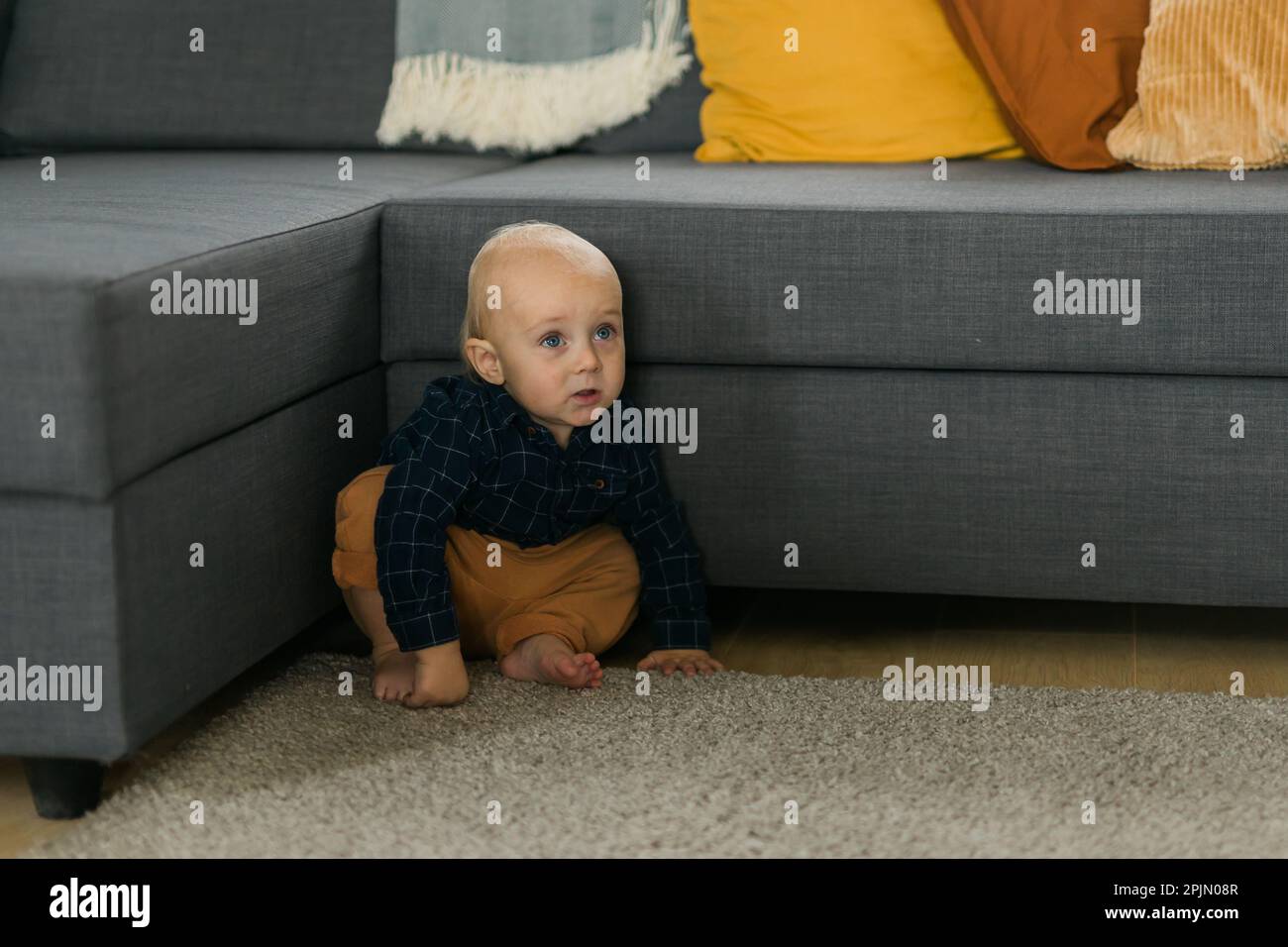 Frustrated scared toddler boy hiding behind a sofa copy space - concept ...