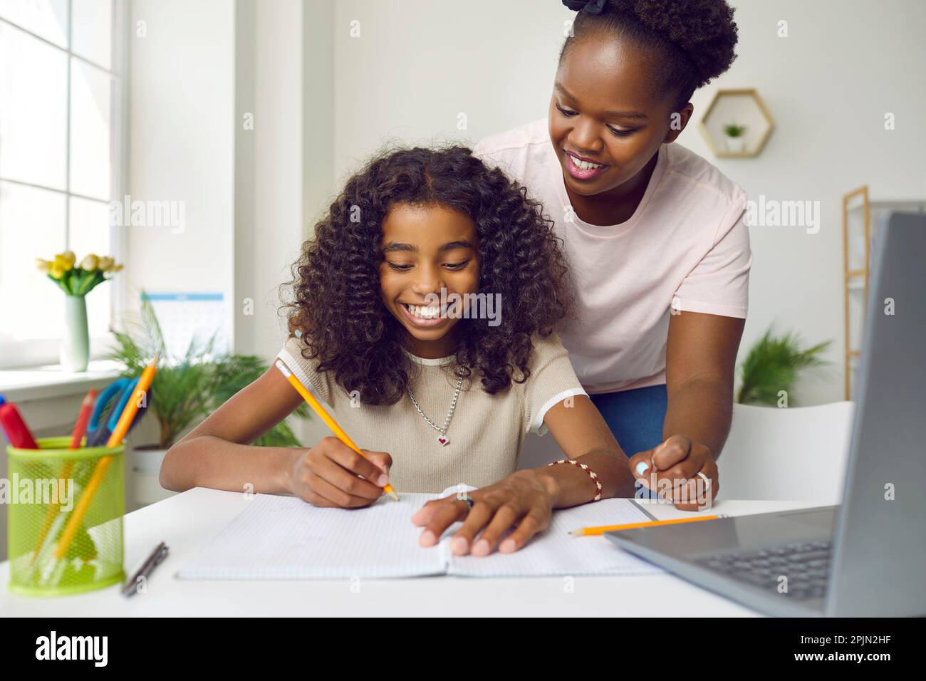 Happy mother looks over her smiling daughters shoulder into workbook ...