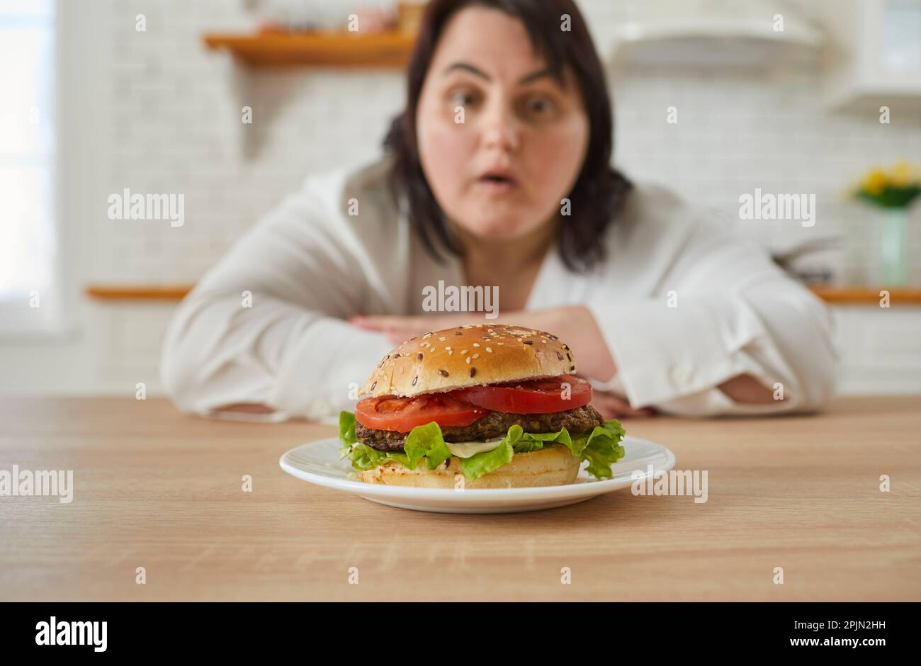 Young fat excited woman sitting at the table in kitchen looking at the ...