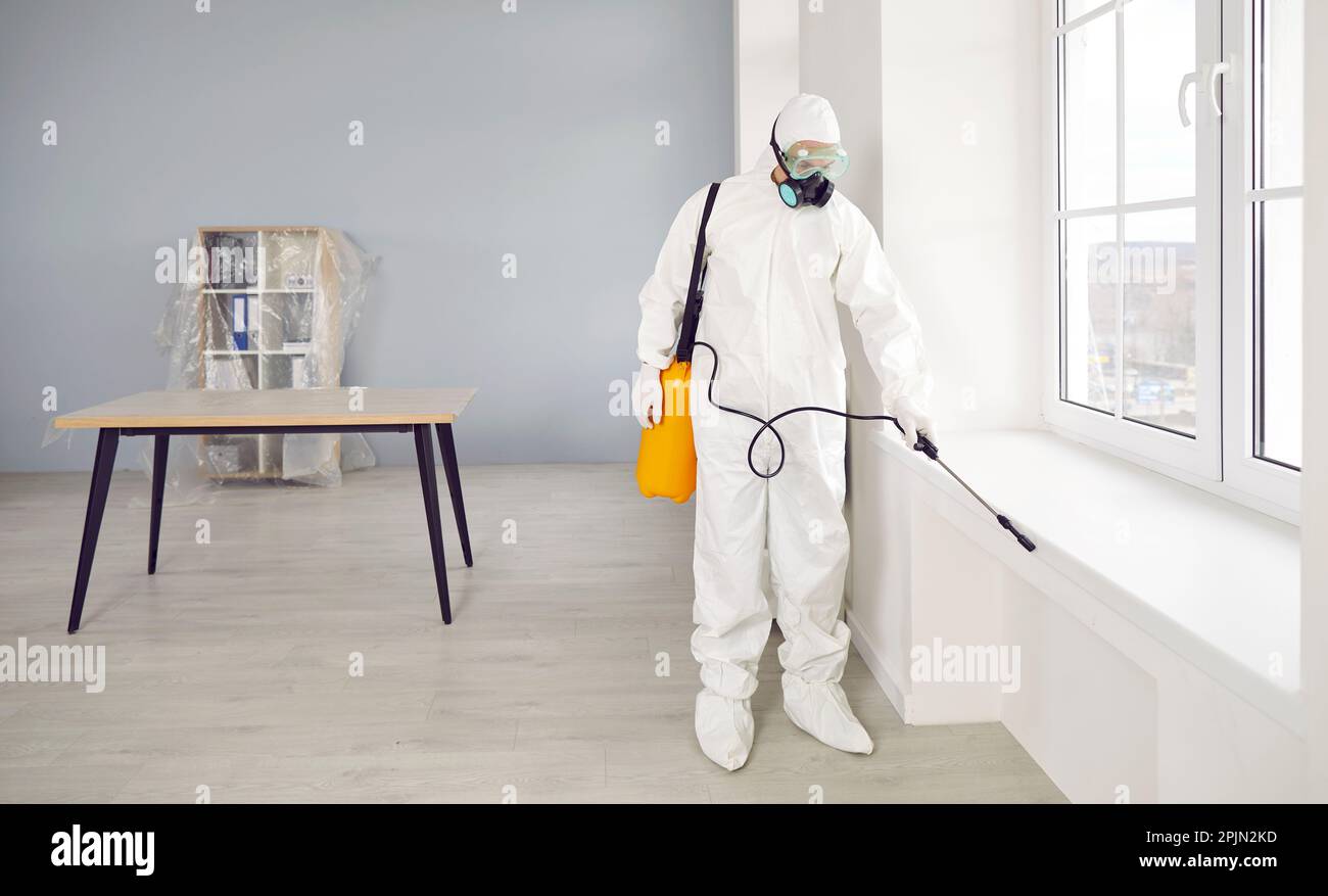 Man wearing protective ppe suit, glasses and face mask disinfecting ...
