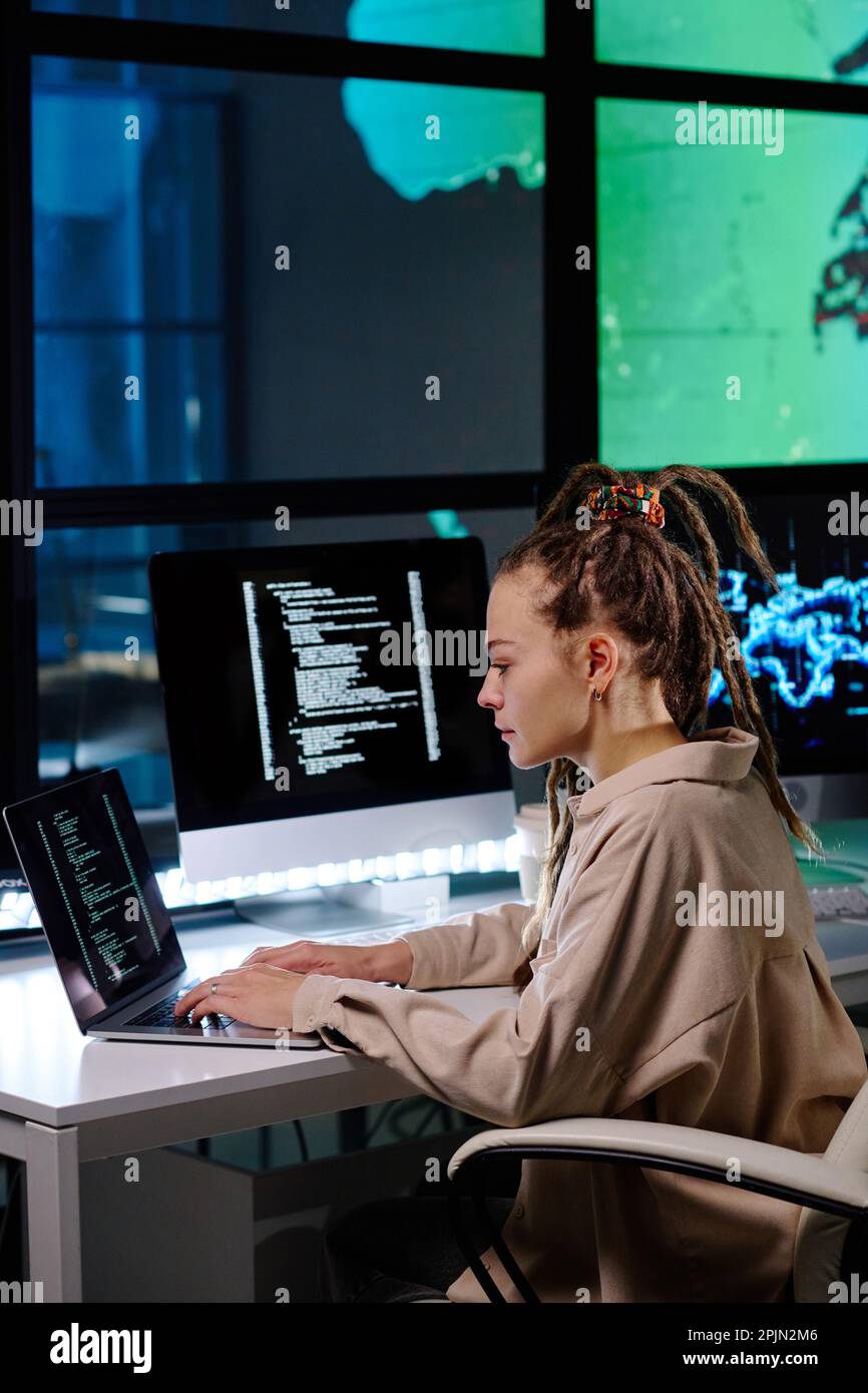 Side view of young female IT support manager with dreadlocks sitting by ...