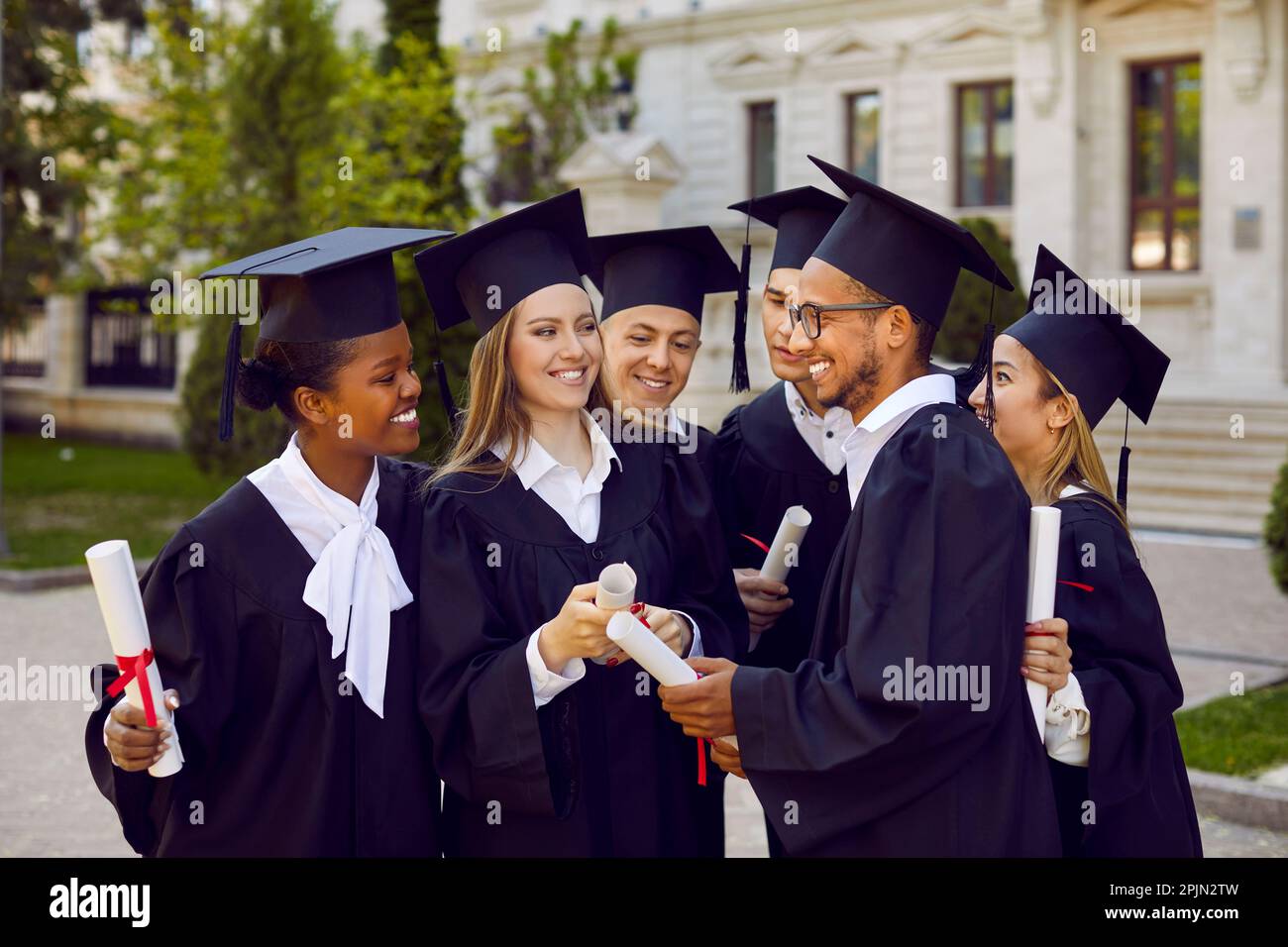 Team of alumni communicate next to university building after graduation ...
